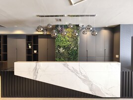Uma mesa de receção com tampo de mármore, um jardim vertical verde e um teto com luminárias esféricas pendentes.