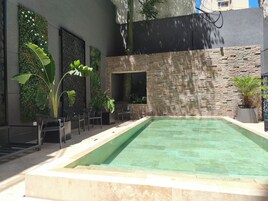 Uma área de piscina moderna ao ar livre, com muro de pedra, assentos e vegetação exuberante.