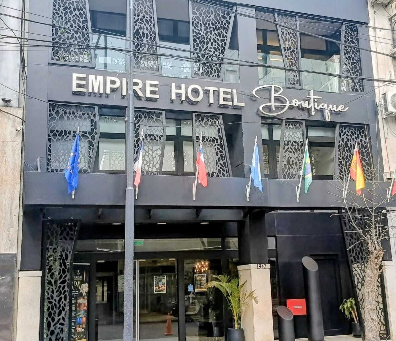 Exterior do Hotel Boutique Empire, com fachada moderna, padrões decorativos nas janelas e diversas bandeiras hasteadas.