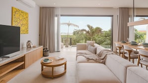 Uma sala de estar moderna com televisão de tela plana, mesa de centro de madeira, sofá e área de jantar com mesa posta para dois.