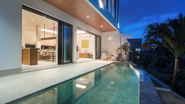 Uma casa moderna com piscina coberta por vidro, área de jantar e cozinha visíveis através das portas de vidro.