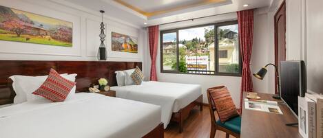 Quarto de hotel com duas camas, uma escrivaninha com cadeira, televisão e janela com vista exterior.
