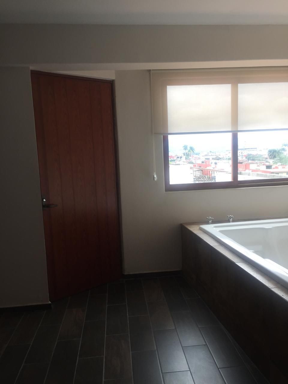 Um banheiro com banheira, janela com vista para edifícios e porta de madeira.