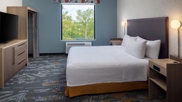 Quarto de hotel com cama, mesas de cabeceira, televisão e janela com vista para árvores.