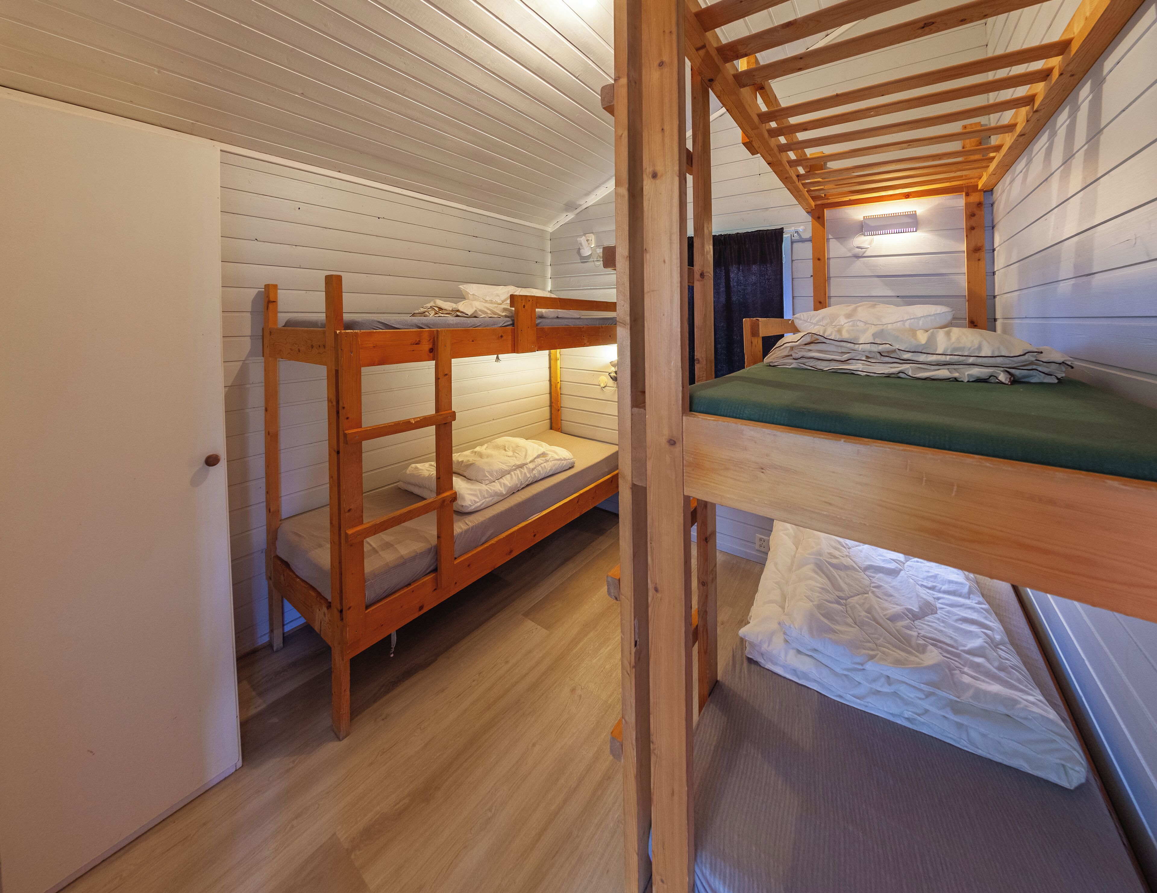 Quarto com beliches de madeira, paredes brancas e piso de madeira.