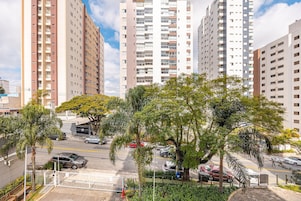Um edifício residencial alto com várias varandas, área de estacionamento com carros e vegetação ao redor.