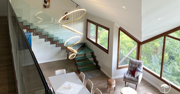 Interior moderno com escada, área de refeições e grandes janelas com vista para o verde.