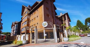 Edifício residencial de vários andares com entrada protegida por portão, grandes janelas e placa indicando localização por tempo limitado.