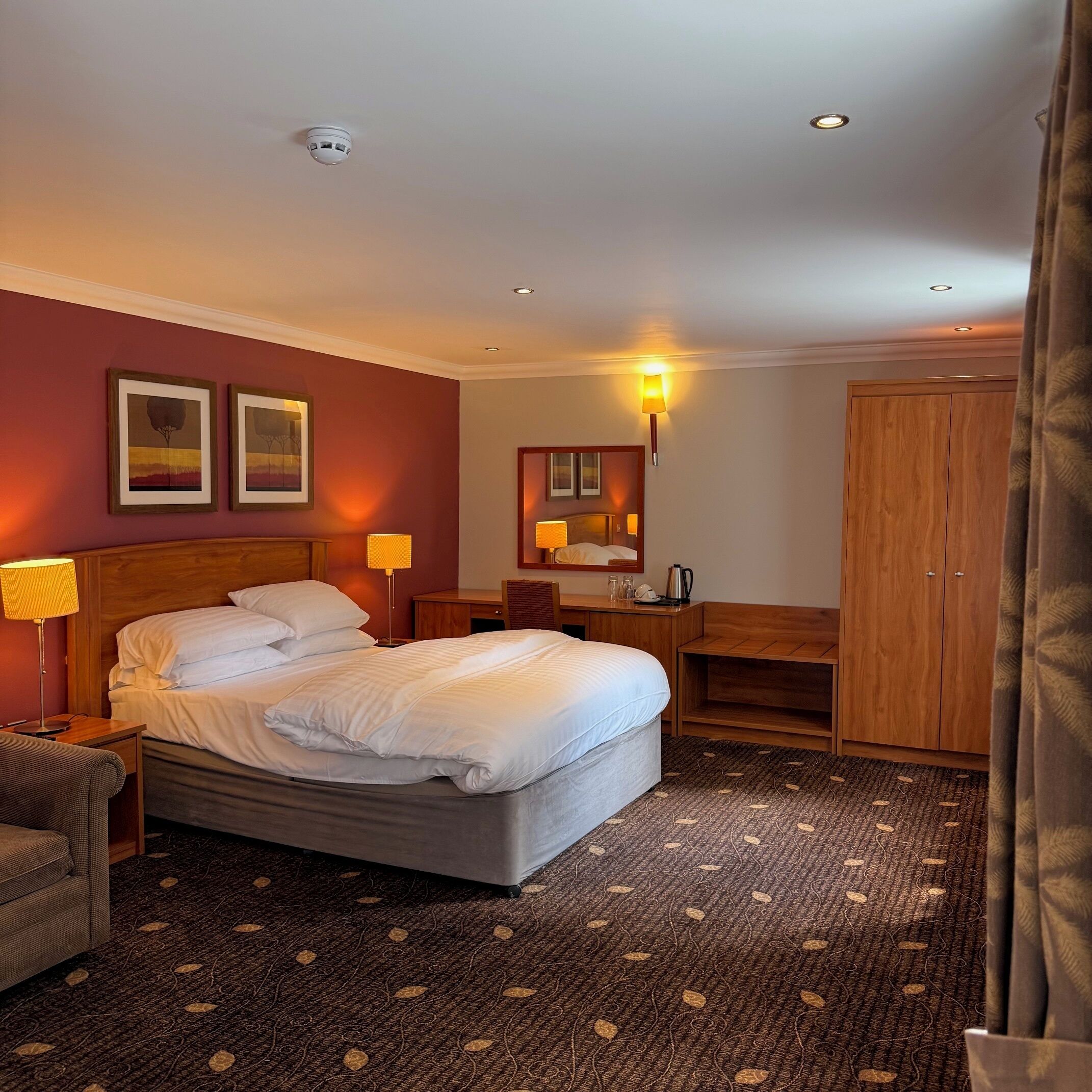 Quarto de hotel com cama, mesas de cabeceira, escrivaninha, cadeira, guarda-roupa e espelho.