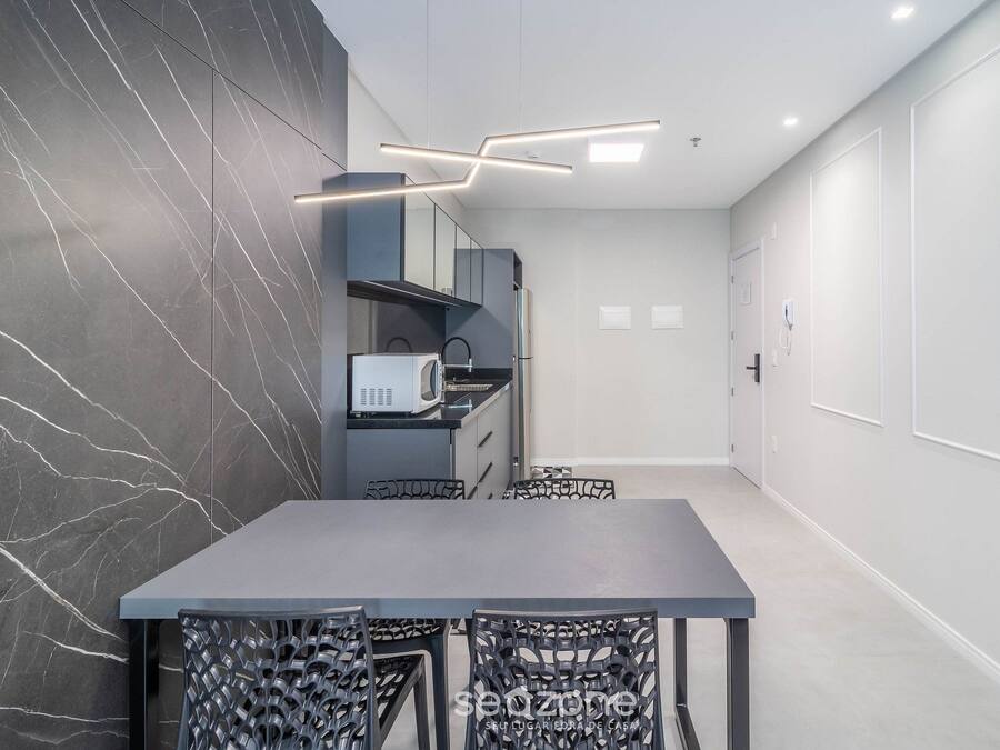 Uma cozinha moderna com revestimento de mármore escuro, micro-ondas embutido e uma luminária elegante.