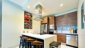 Cozinha moderna com ilha central, banquetas, eletrodomésticos de aço inoxidável e um detalhe decorativo na parede.