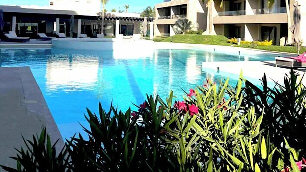 Um hotel moderno com piscina, várias varandas e palmeiras.