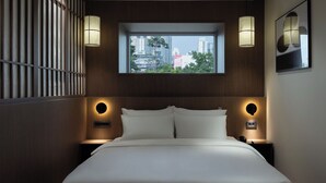 Quarto de hotel com uma cama grande, duas mesas de cabeceira, uma janela com vista para a cidade e iluminação na parede.