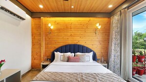 Quarto com cabeceira de madeira, cama grande com várias almofadas, mesa de cabeceira e janela com vista para o verde.