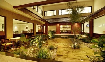 Um pátio interno amplo com piso de azulejos, áreas de estar e uma árvore central.