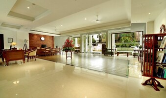 Um hall amplo com piso lustroso, mobiliário de madeira, uma planta grande e uma estante de livros.