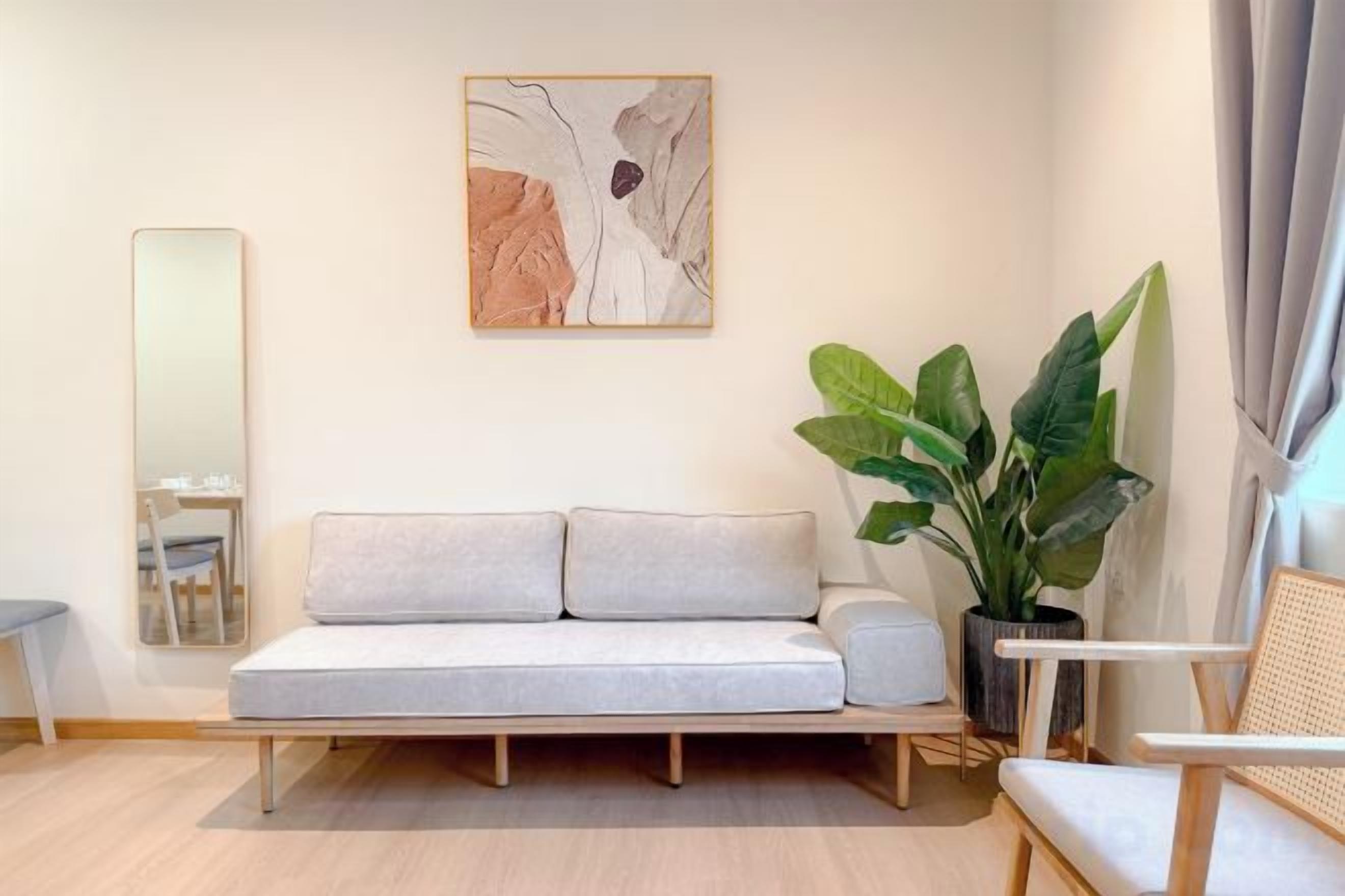 Uma sala de estar moderna com um sofá, uma poltrona, uma planta grande e uma obra de arte na parede.