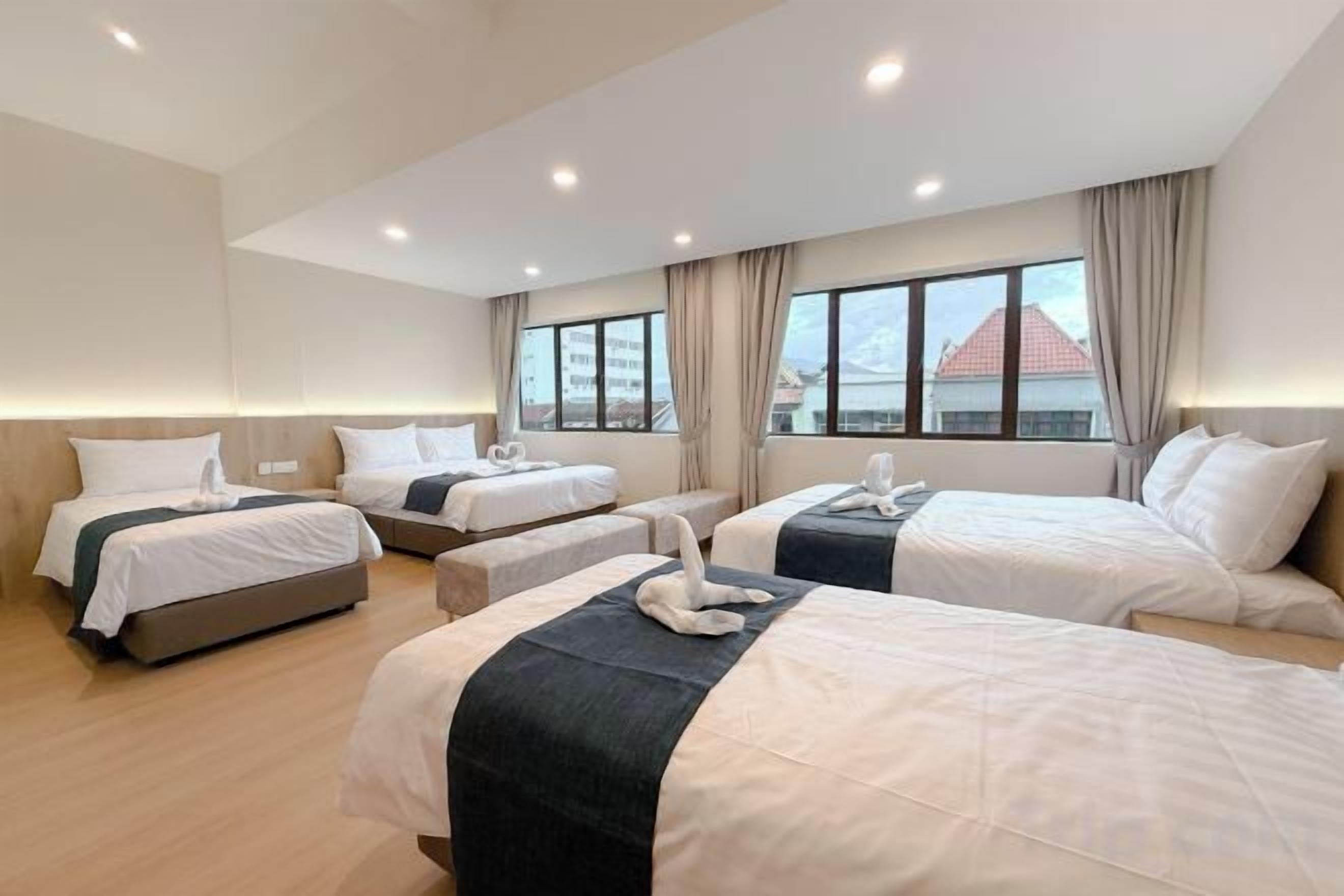 Quarto de hotel com três camas, uma janela grande e vista para a cidade.