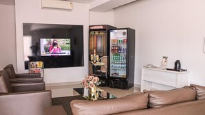 Uma sala de estar moderna com televisão de tela plana, minibar, área de estar com sofás de couro e um vaso decorativo.