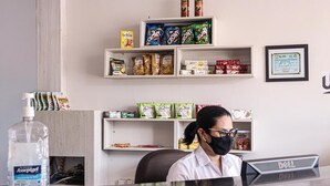 Uma receção com um computador Dell, prateleiras repletas de snacks e bebidas, e um certificado emoldurado na parede.