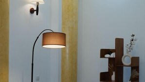 Quarto com luminária de chão, luminária na parede e prateleira de madeira com objetos decorativos.