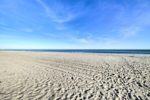 Uma extensa praia de areia com marcas de pneus visíveis e um céu azul límpido.