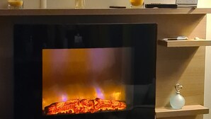 Uma televisão de tela plana fixada numa parede de madeira, com uma lareira abaixo.
