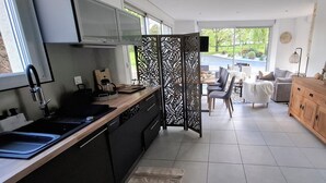 Uma cozinha moderna com uma ilha grande, área de refeições com vista e sala de estar com sofá e televisão.