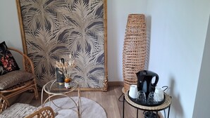 Um quarto aconchegante com uma cadeira de vime, uma mesa de vidro redonda, um espelho grande e uma cesta trançada.