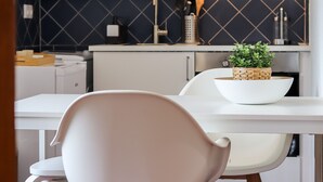Uma cozinha moderna com bancada branca, uma cadeira branca e um pequeno vaso com planta.