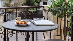 Mesa redonda com uma chávena, doces e um livro aberto numa varanda.
