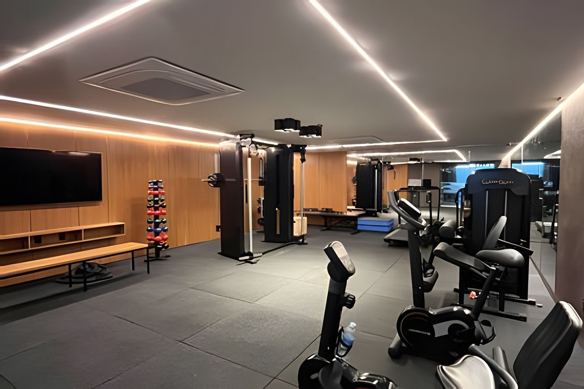 Uma academia moderna com diversos equipamentos de exercício, um banco e uma TV fixada na parede.