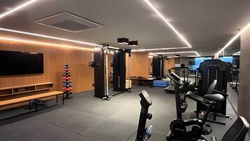 Uma academia moderna com diversos equipamentos de exercício, um banco e uma TV fixada na parede.