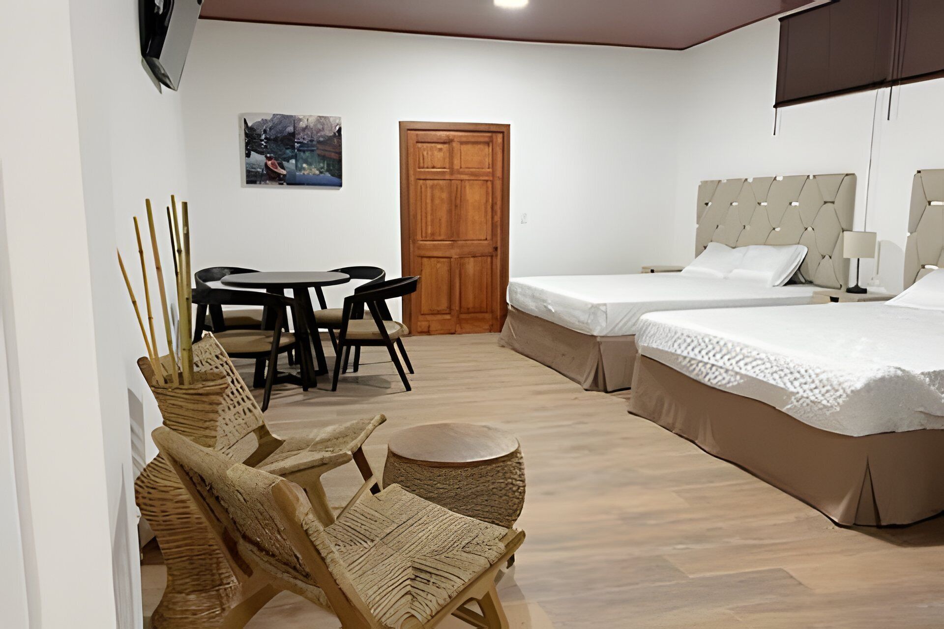 Quarto com duas camas, uma mesa de jantar com cadeiras, uma porta de madeira e um quadro na parede.