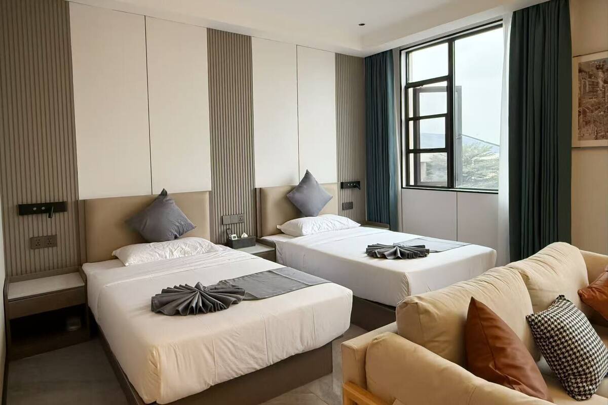 Quarto de hotel com duas camas, um sofá e uma janela grande com cortinas.