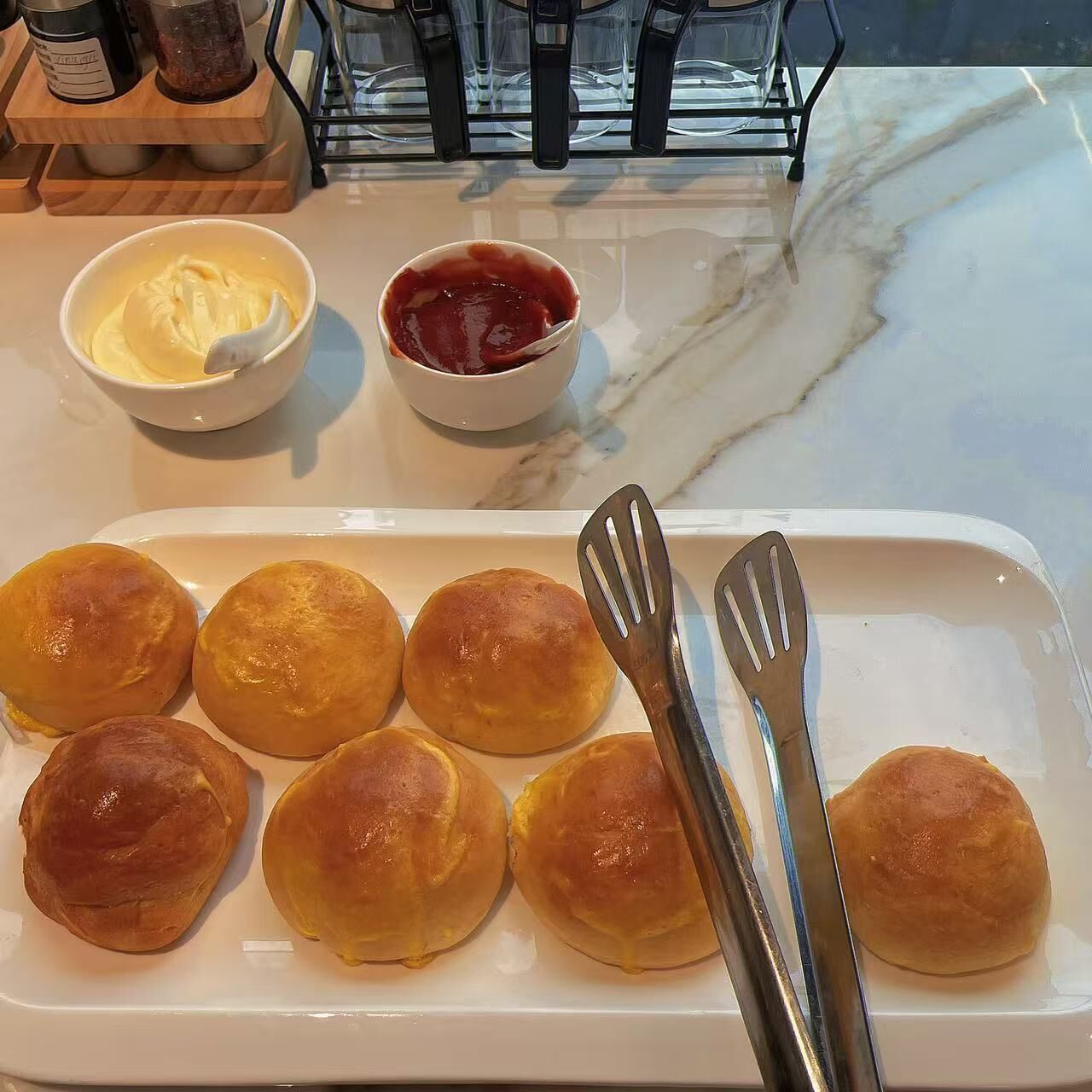 Uma travessa com pães de jantar dourados, manteiga e geleia sobre um balcão de mármore.