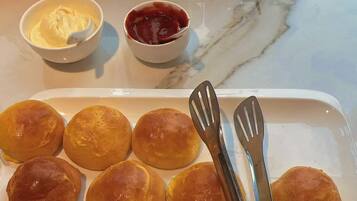 Uma travessa com pães de jantar dourados, manteiga e geleia sobre um balcão de mármore.