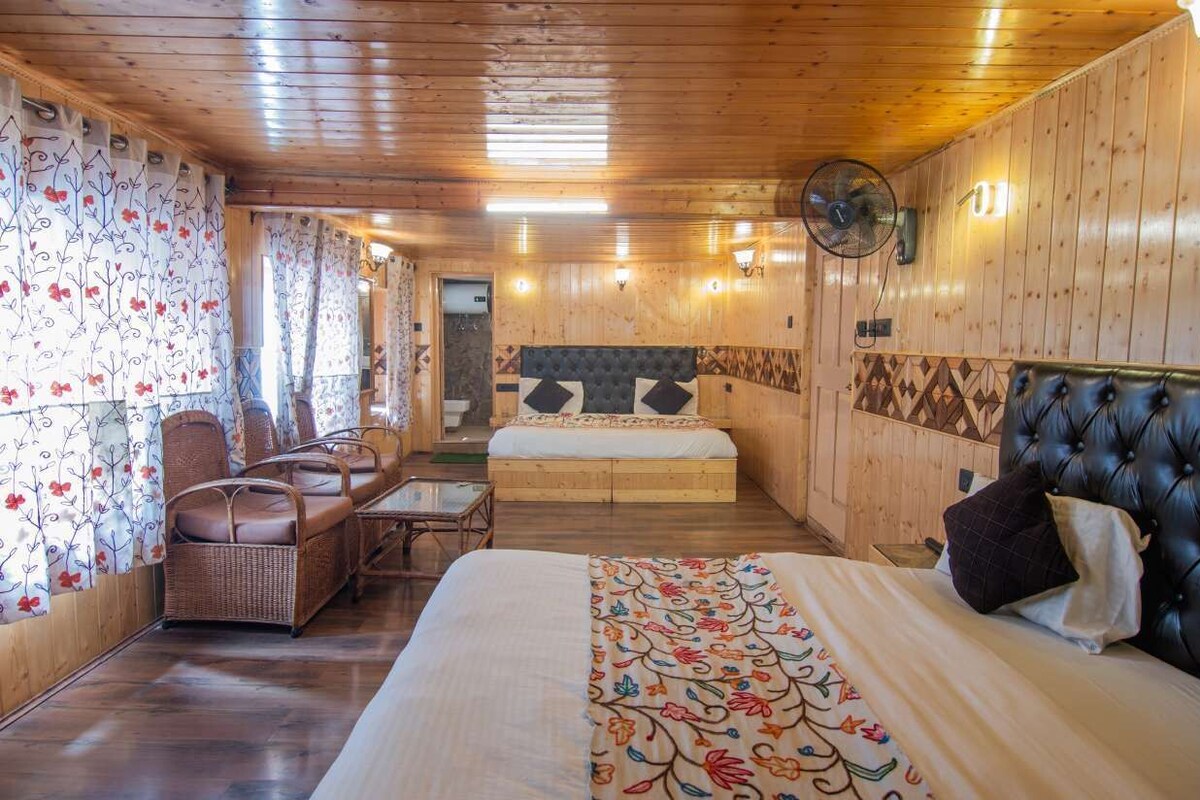Quarto estilo cabana de madeira com uma cama, duas cadeiras de vime, uma mesinha e um ventilador.