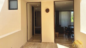 Um corredor com uma porta que dá para uma sala de jantar. Há uma pequena janela na parede esquerda e uma porta com placa de identificação na parede direita.
