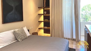 Quarto de hotel moderno com uma cama grande, um quadro abstrato na parede, estantes embutidas com objetos decorativos e vista através de cortinas leves.