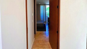 Um corredor com uma porta de madeira, uma placa na parede e uma cama ao fundo.