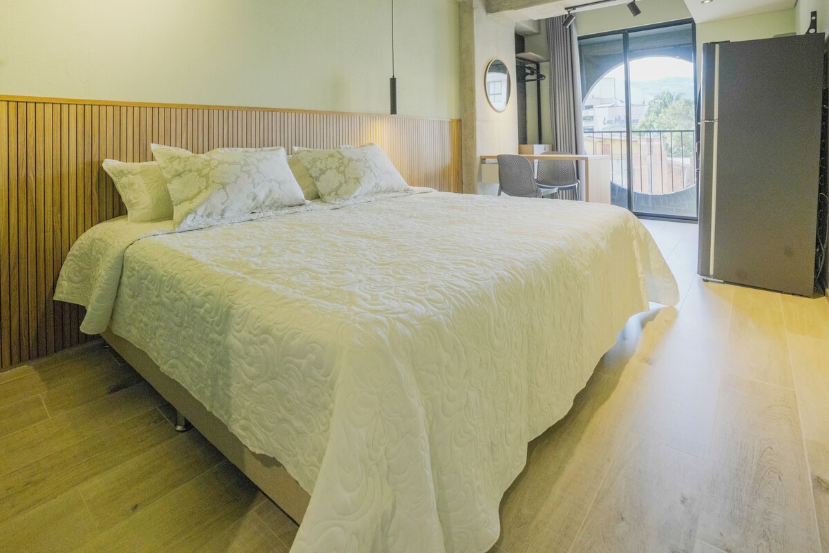 Quarto de hotel com cama grande, escrivaninha, cadeira, frigorífico e vista para o exterior.
