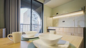 Cozinha moderna com uma janela grande, uma mesa de jantar com tigelas e xícaras, e vista para edifícios lá fora.