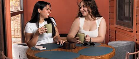 Duas mulheres sentadas numa mesa redonda de madeira, com um livro pequeno e uma caixa de madeira.