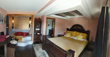 Um quarto com uma cama grande, uma cômoda de madeira, uma cadeira vermelha, uma mesa pequena com um narguilé e um banheiro visível através de uma porta aberta.
