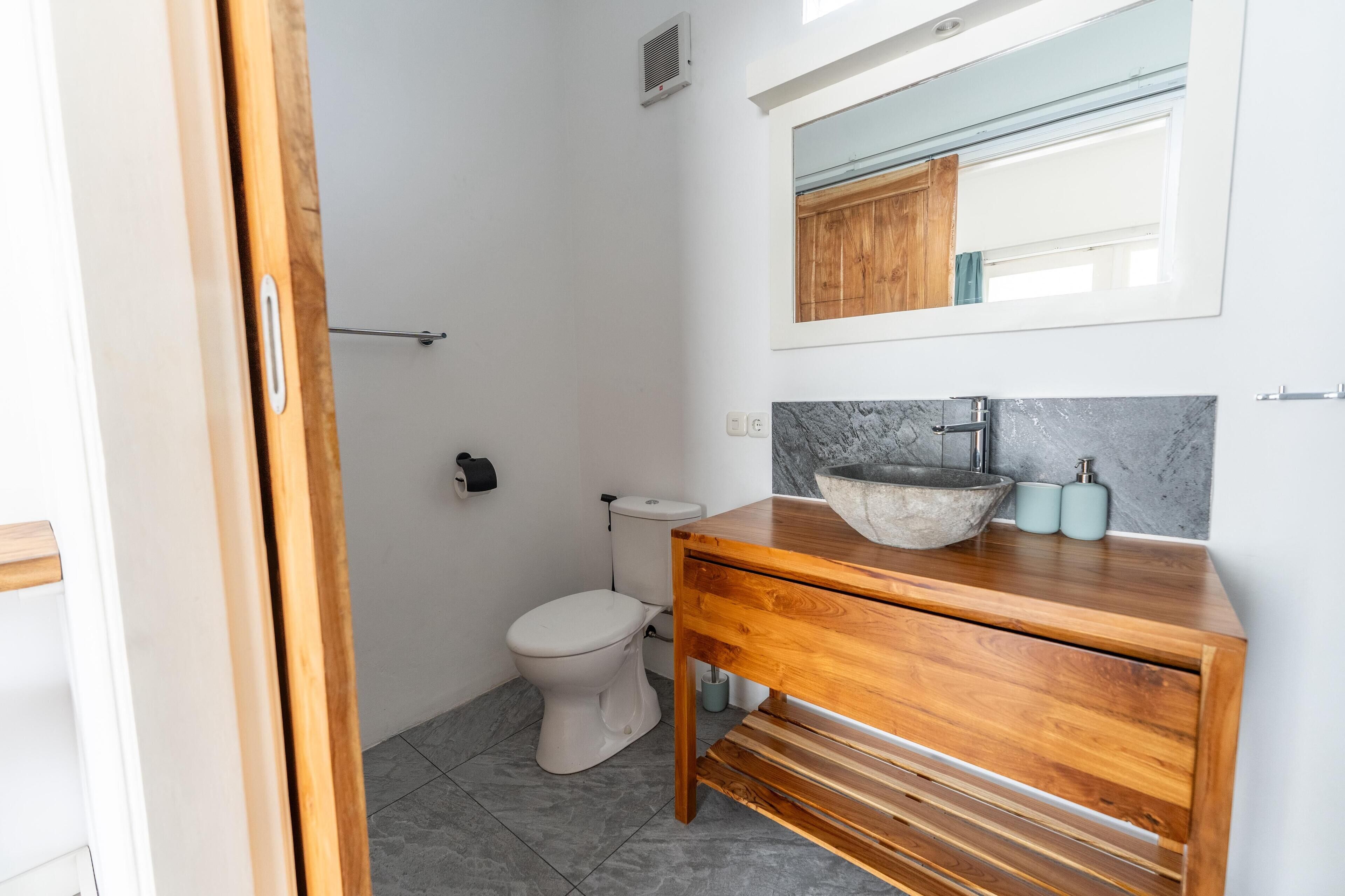 Uma casa de banho com toucador de madeira, lavatório de mármore e sanita.