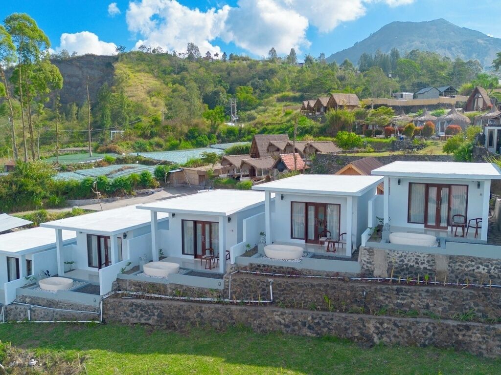 Um resort moderno com edifícios brancos, área de estar externa e vista para uma paisagem verdejante com montanhas ao fundo.