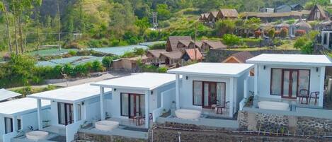 Um resort moderno com edifícios brancos, área de estar externa e vista para uma paisagem verdejante com montanhas ao fundo.