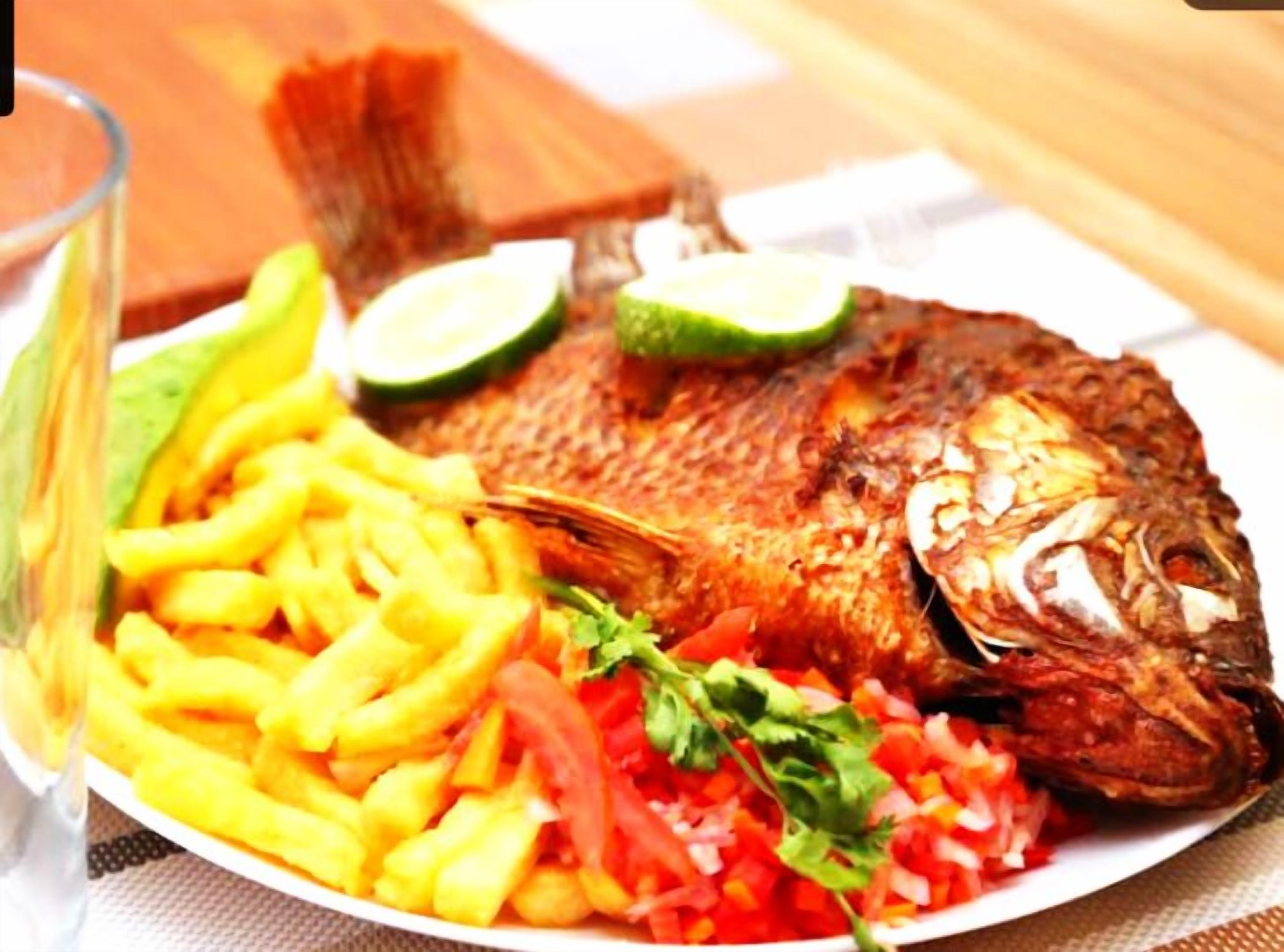 Prato com um peixe frito inteiro, batatas fritas, tomate picado e um gomo de limão.