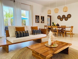 Uma sala de estar moderna com sofá, mesa de centro de madeira, mesa de jantar com cadeiras e arte decorativa na parede.